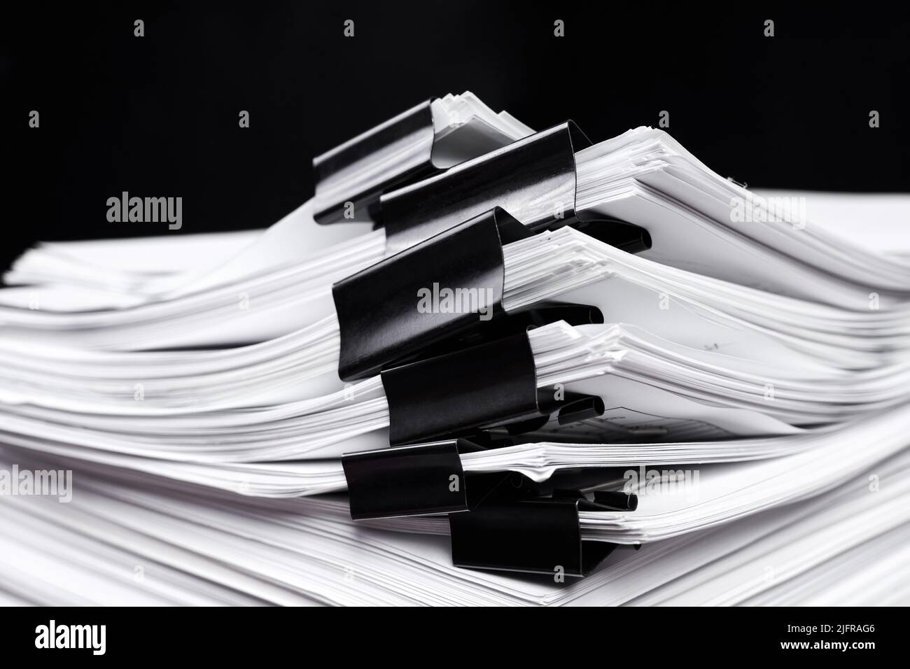A stack of office papers, some of which are fastened with black binders ...