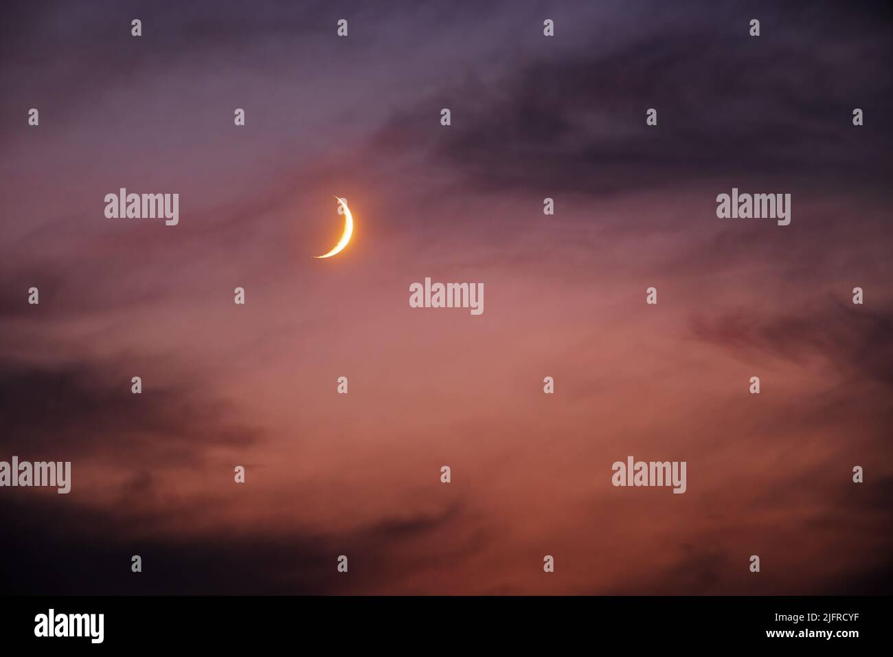 Growing moon in dramatic night sky among clouds. Warm colors of summer ...