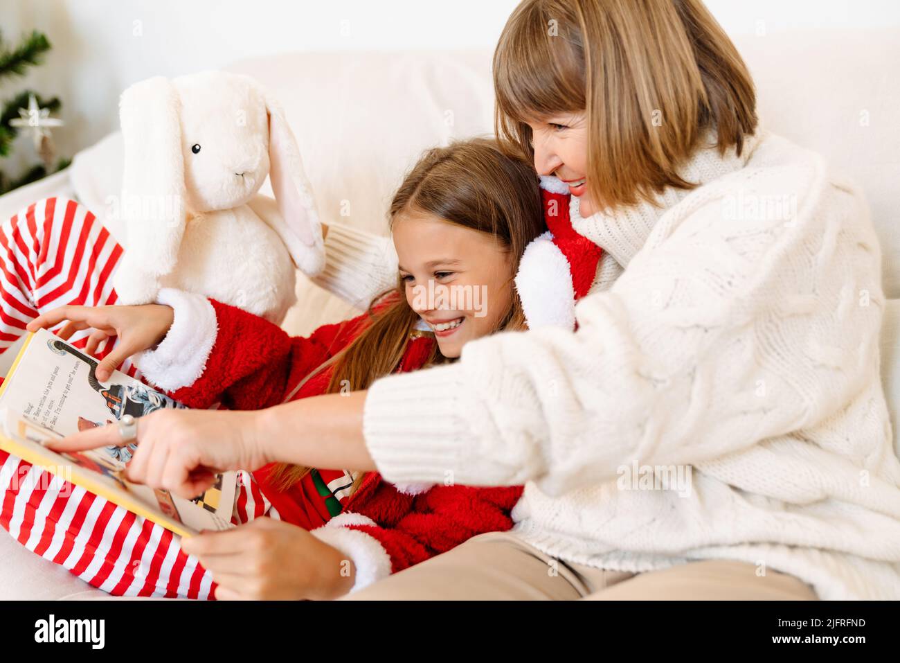 White girl reading book with her grandmother while sitting on sofa at ...