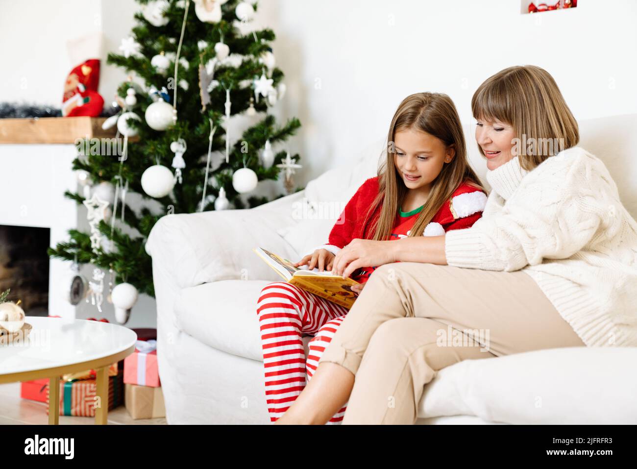 White girl reading book with her grandmother while sitting on sofa at ...