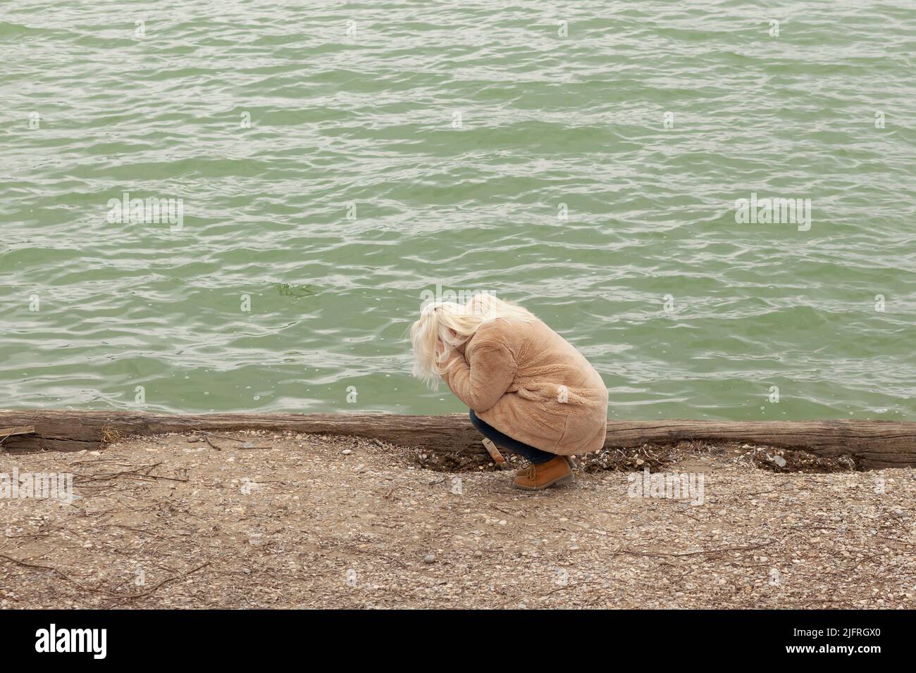 Woman crouching by the water, hands on heads, desperate and afraid ...
