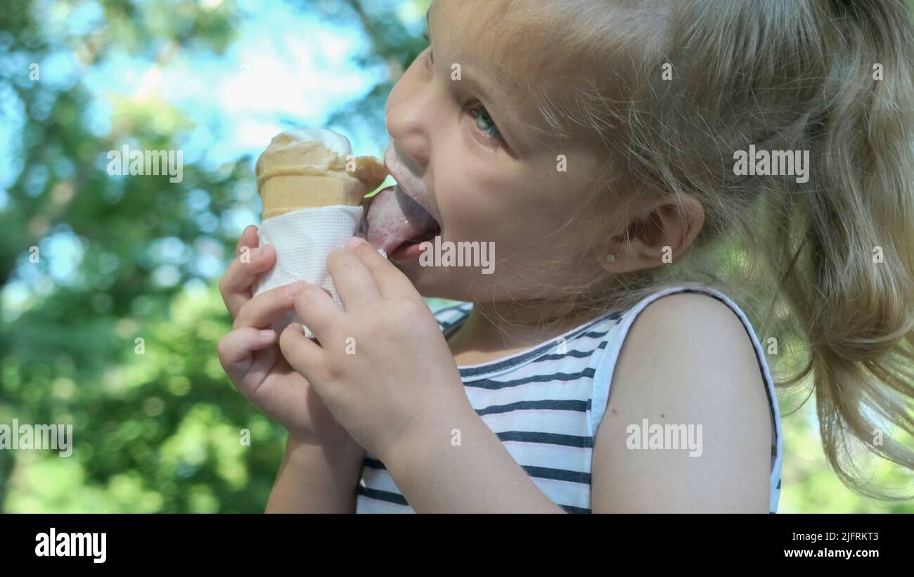 Cute little girl eats ice cream outside. Close-up portrait of blonde ...