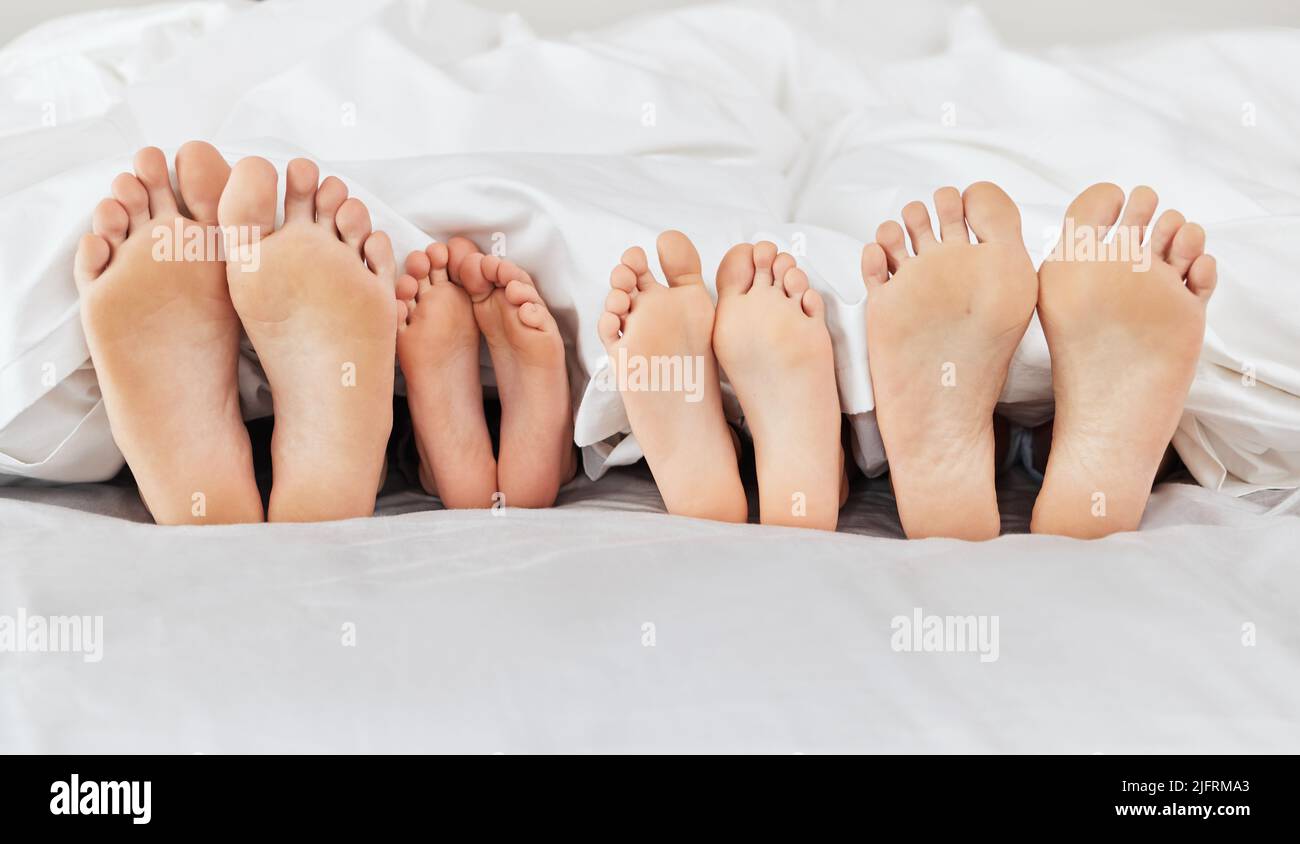 Eight feet resting in love. Shot of a family laying barefoot on a bed ...
