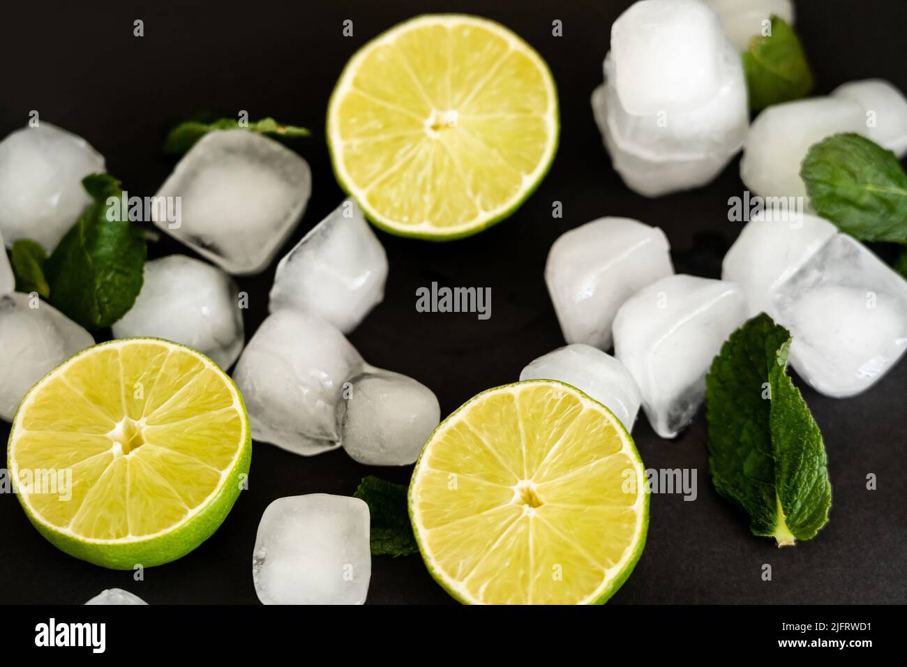 high angle view of melting ice cubes near sliced limes on black ...