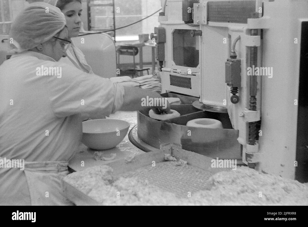 Two women operating an automatic pie press machine in a factory setting ...