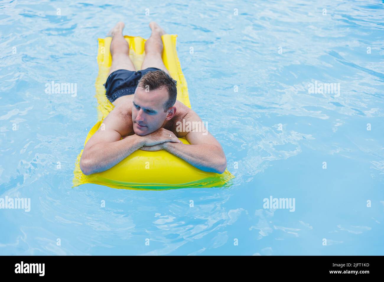 A young man in shorts enjoys the water park floating in an inflatable ...
