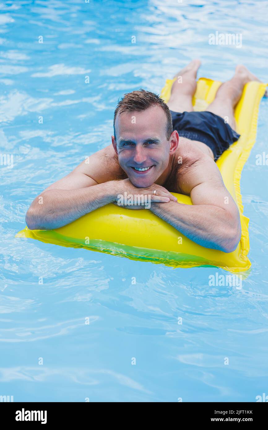 A young man in shorts enjoys the water park floating in an inflatable ...