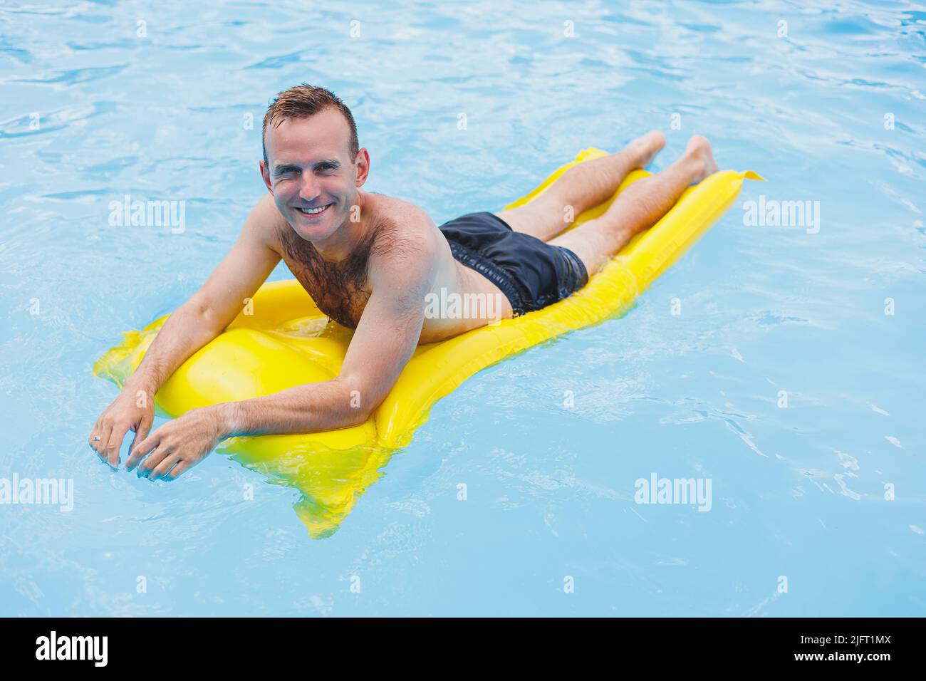 A young man in shorts enjoys the water park floating in an inflatable ...