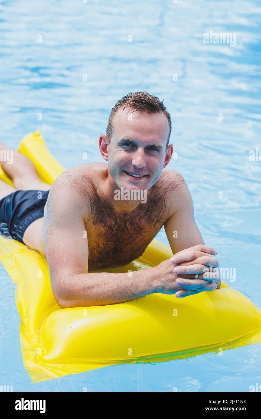 A young man in shorts enjoys the water park floating in an inflatable ...