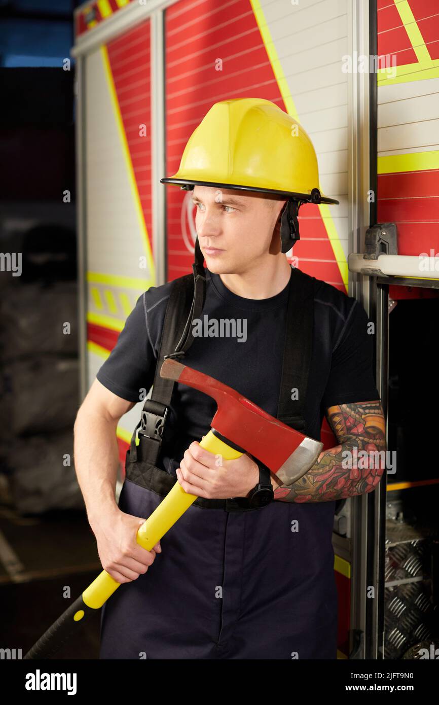 Photo of fireman wearing helmet with ax against fire engine Stock Photo ...