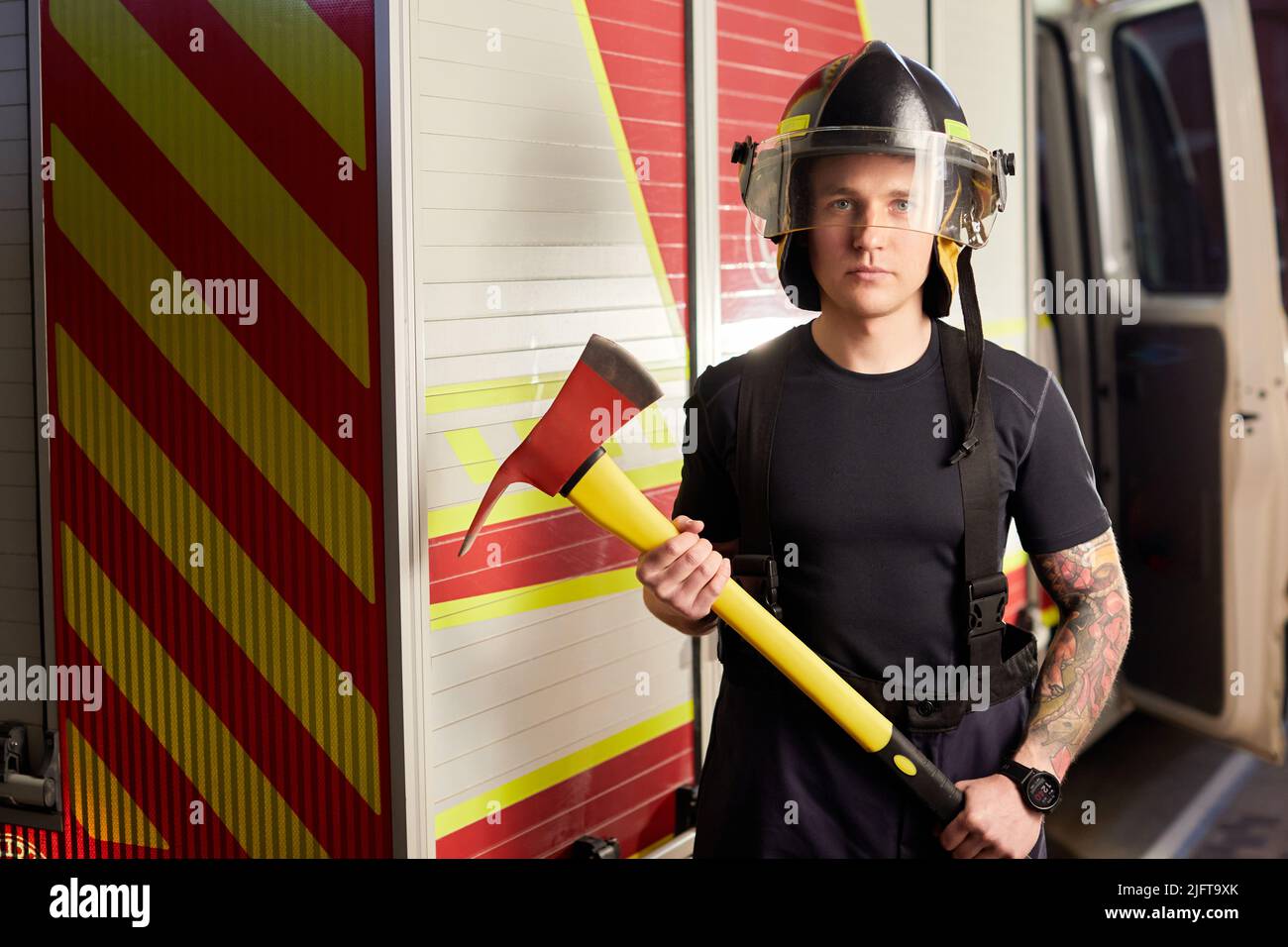 Photo of fireman wearing helmet with ax against fire engine Stock Photo ...