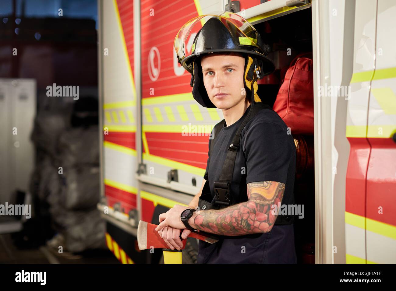 Photo of fireman wearing helmet with ax against fire engine Stock Photo ...