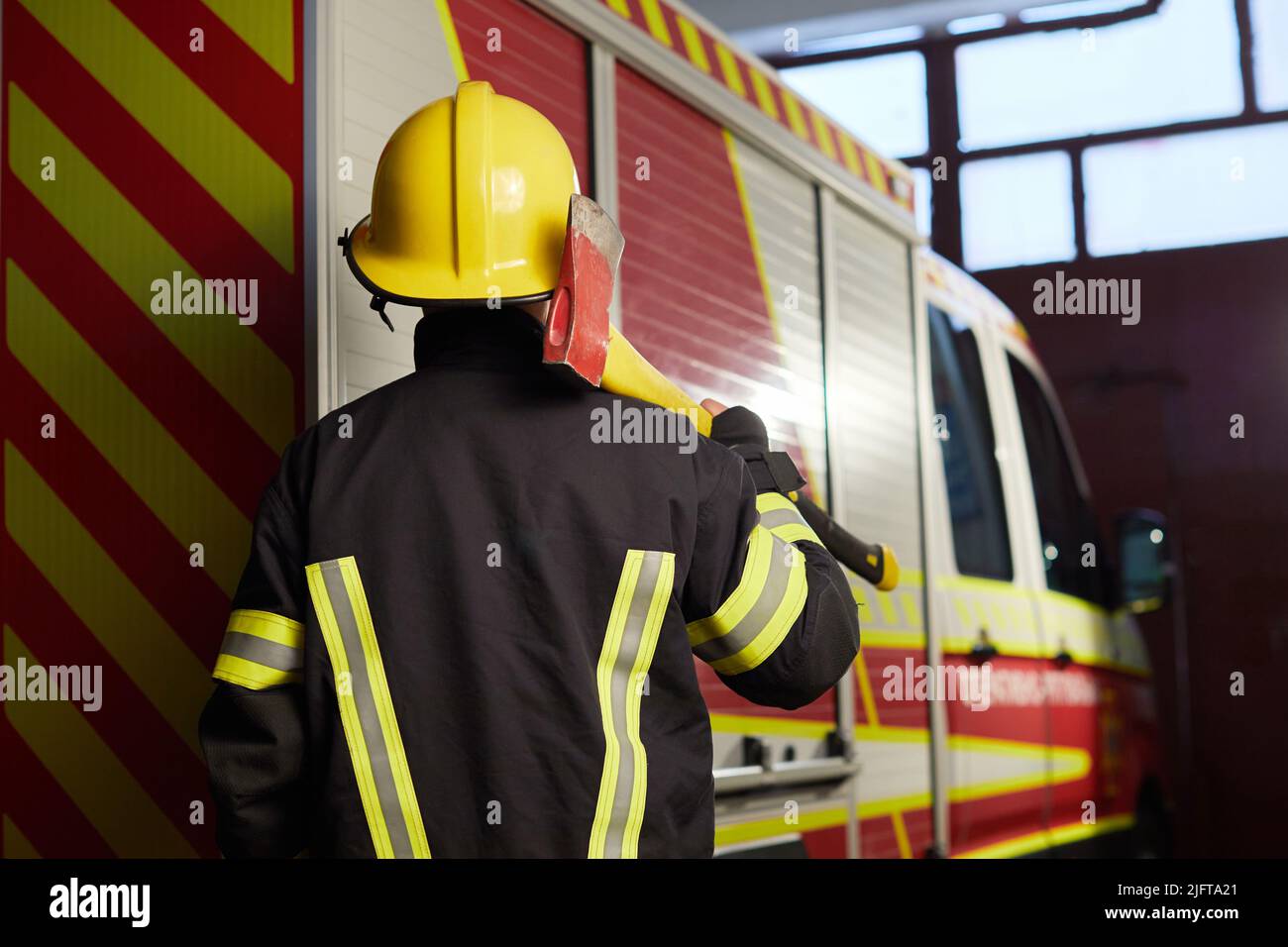 Firefighter fully equipped with helmet and ax in fire truck background ...