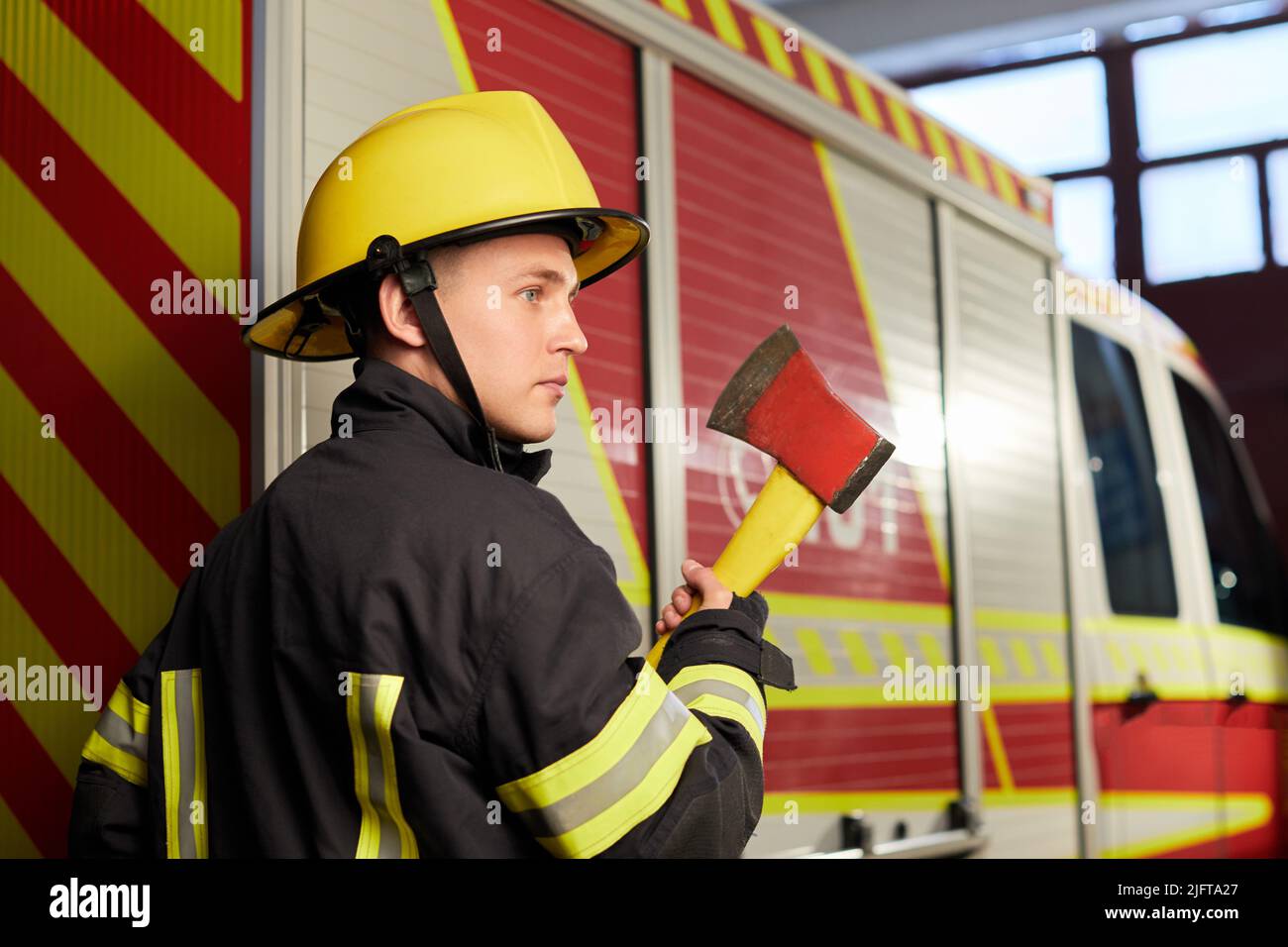 Firefighter fully equipped with helmet and ax in fire truck background ...