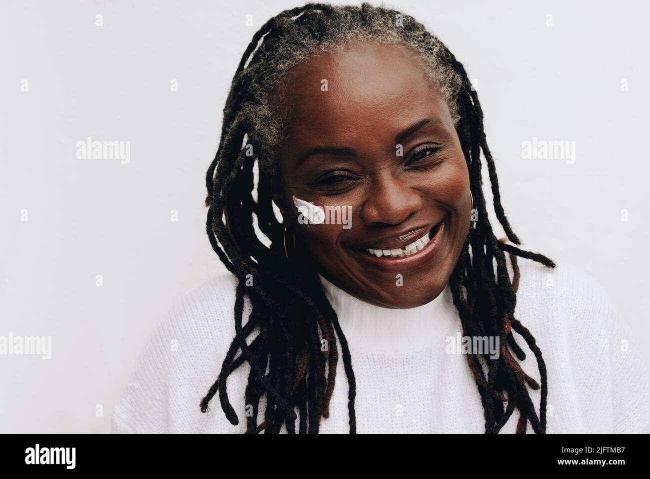 Happy mature woman with dreadlocks applying a beauty cream on her face ...