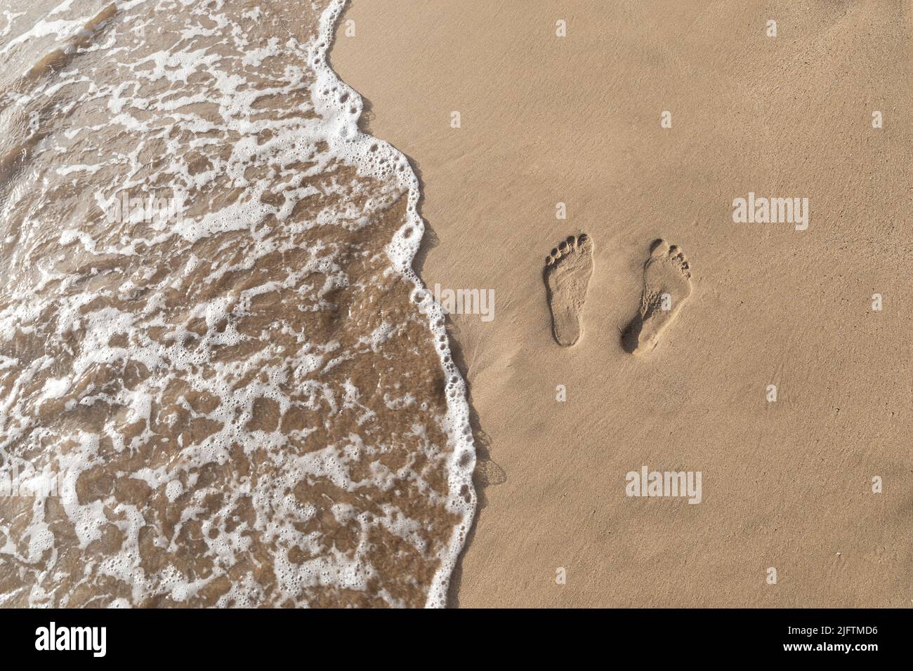 Two footsteps with waves ocean water in the sand on a walk in Maui ...