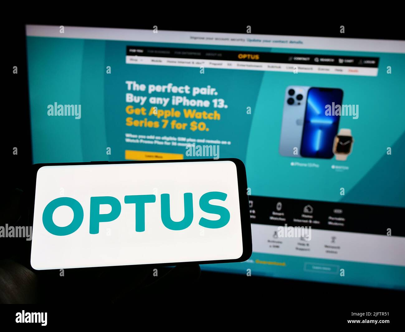 Person holding mobile phone with logo of communications company SingTel Optus Pty. Ltd. on ...