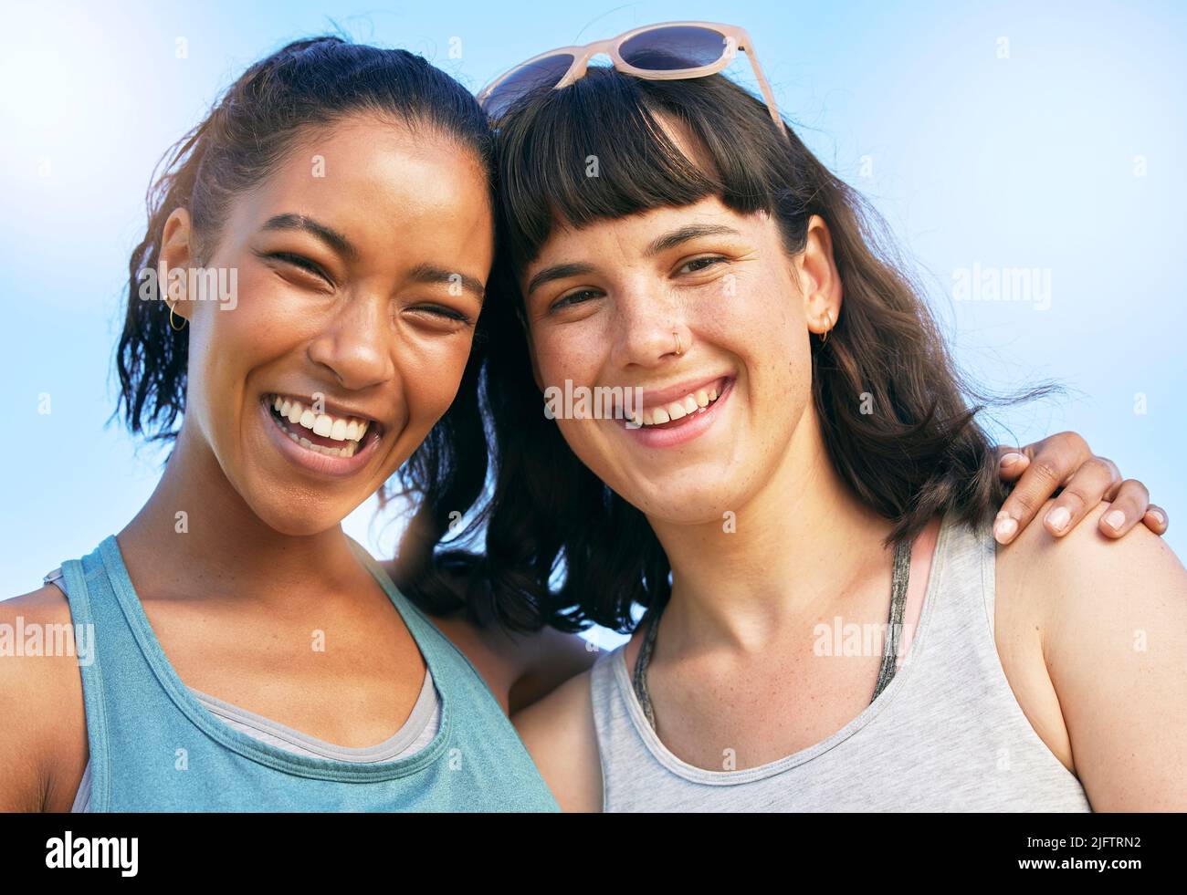 Portrait of two smiling friends embracing while standing together ...