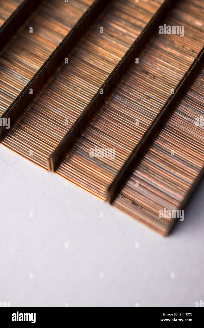 A top view of row of upside-down bronze stapler pins on white table ...