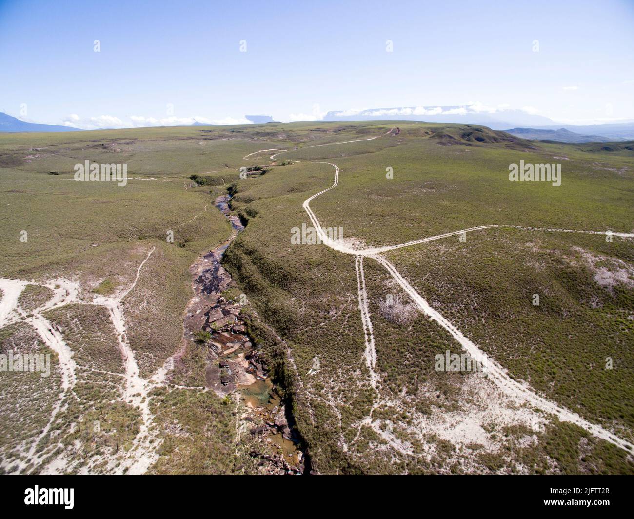 A green landscape with a river with almost no water and snowy patches ...