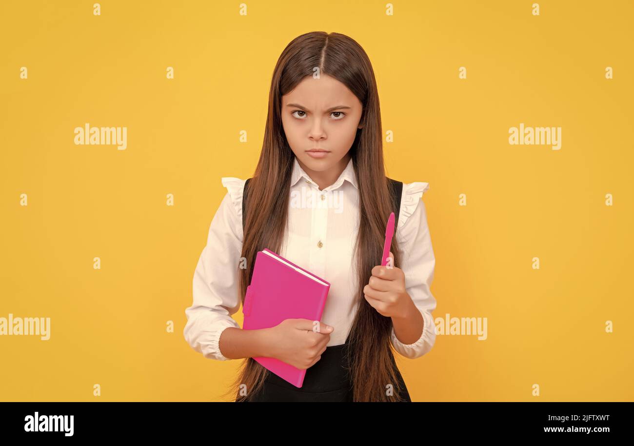 Serious frown child hold school book and pen yellow background ...