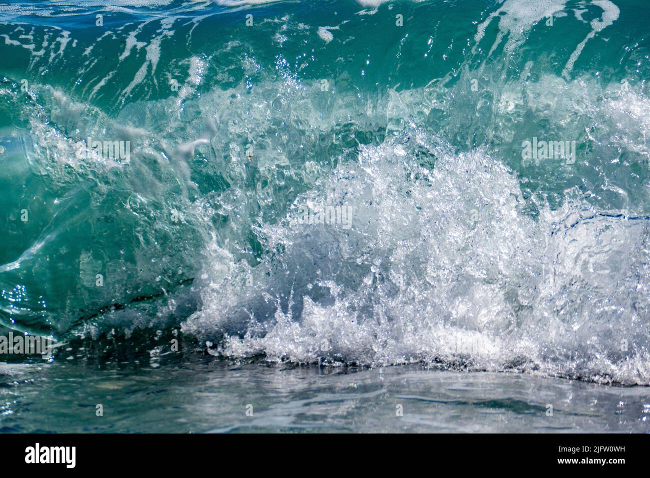 Closeup of the spray of curly turquoise storm waves breaking on sandy ...