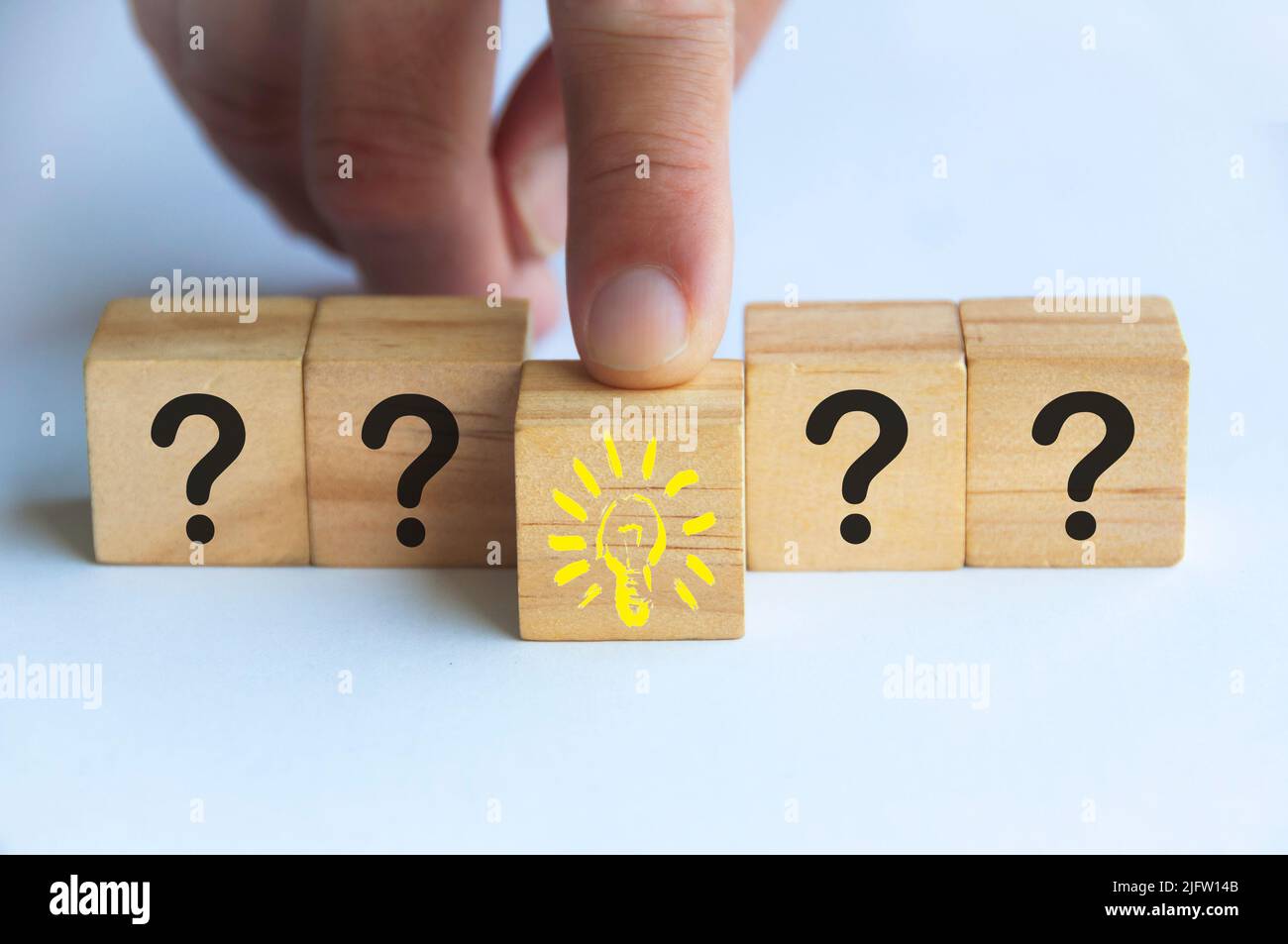 Hand pointing at wooden cube block with light bulb surrounded by ...