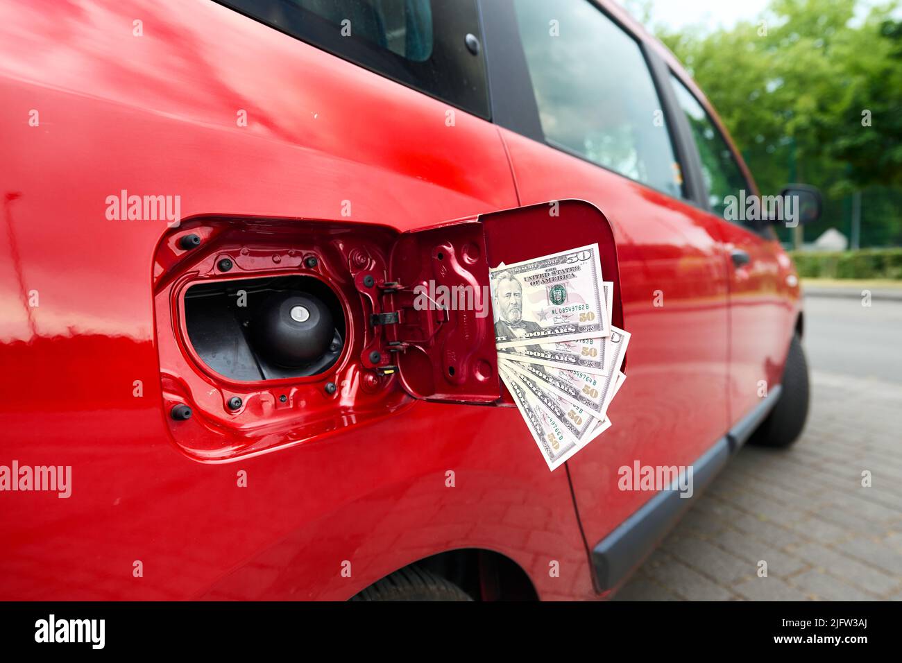 Fifty dollar bills sticking out of an open gas cap on a car, symbol of ...