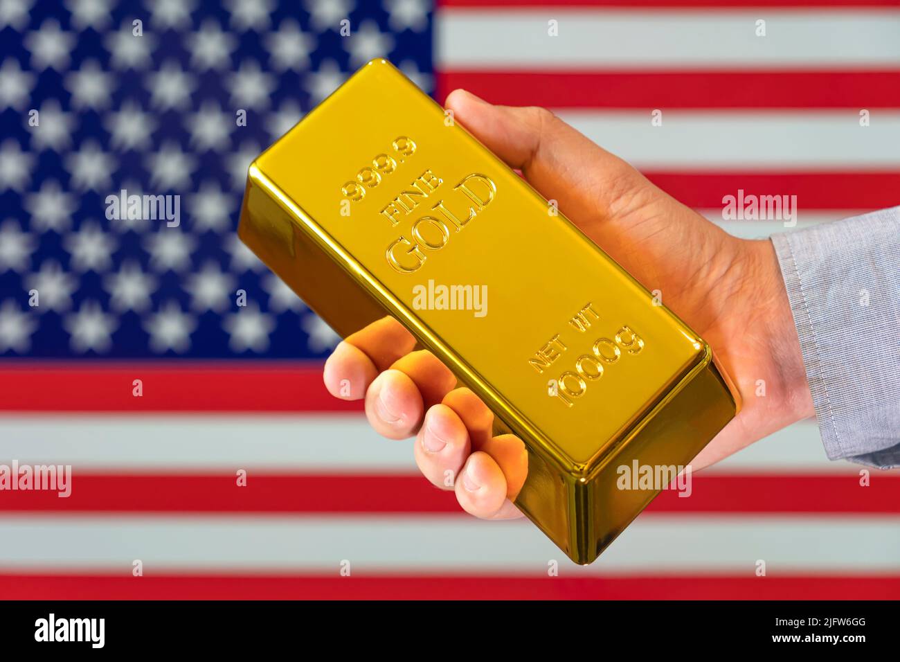 a gold bar in a man's hand on the background of the American flag. America's gold. Trading on ...