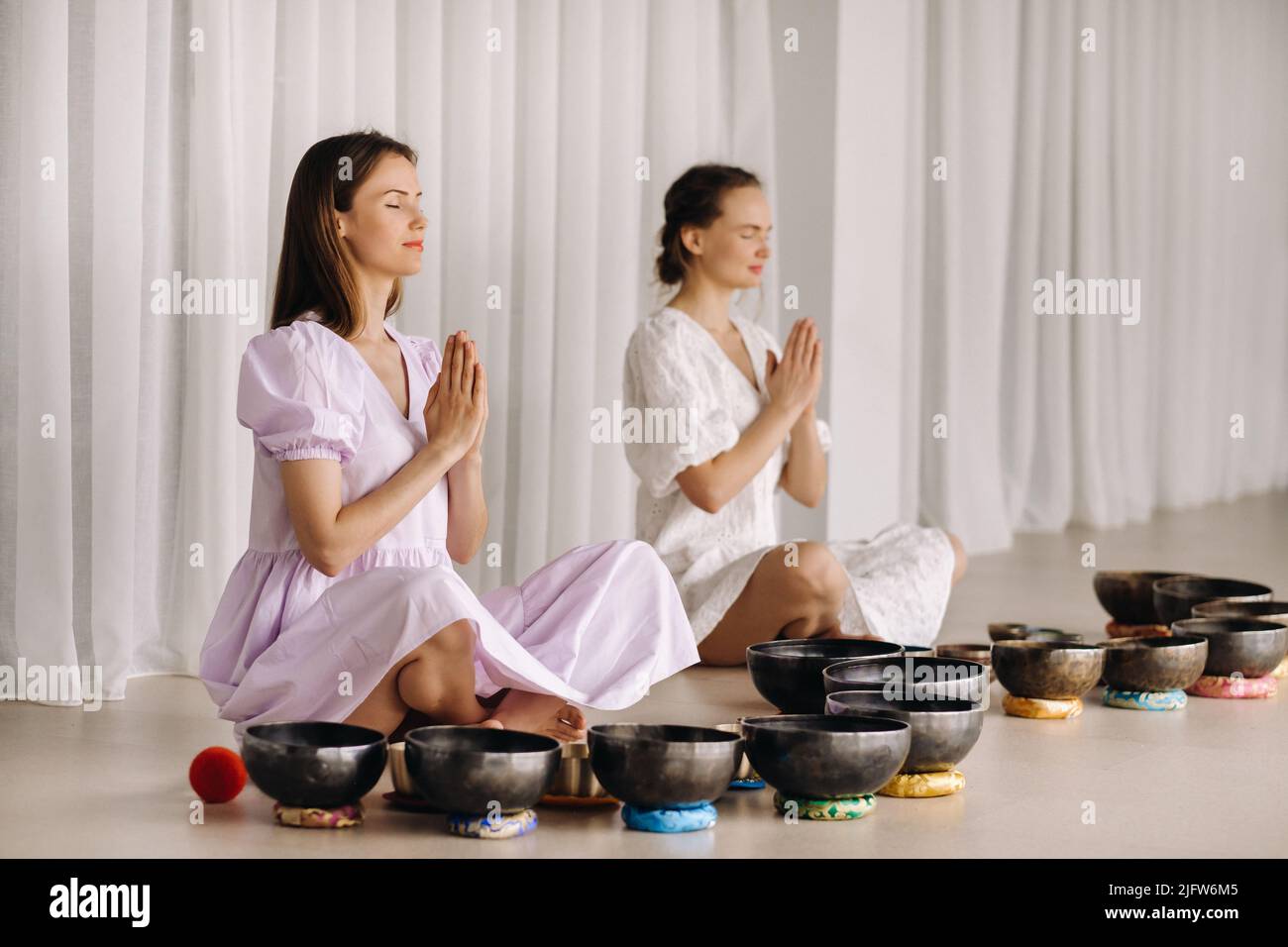 Two women are sitting with Tibetan bowls in the lotus position before a ...