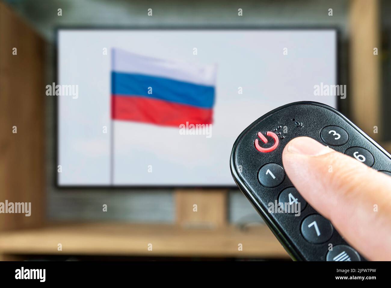 Remote control in a man's hand on the background of a TV and a Russian ...