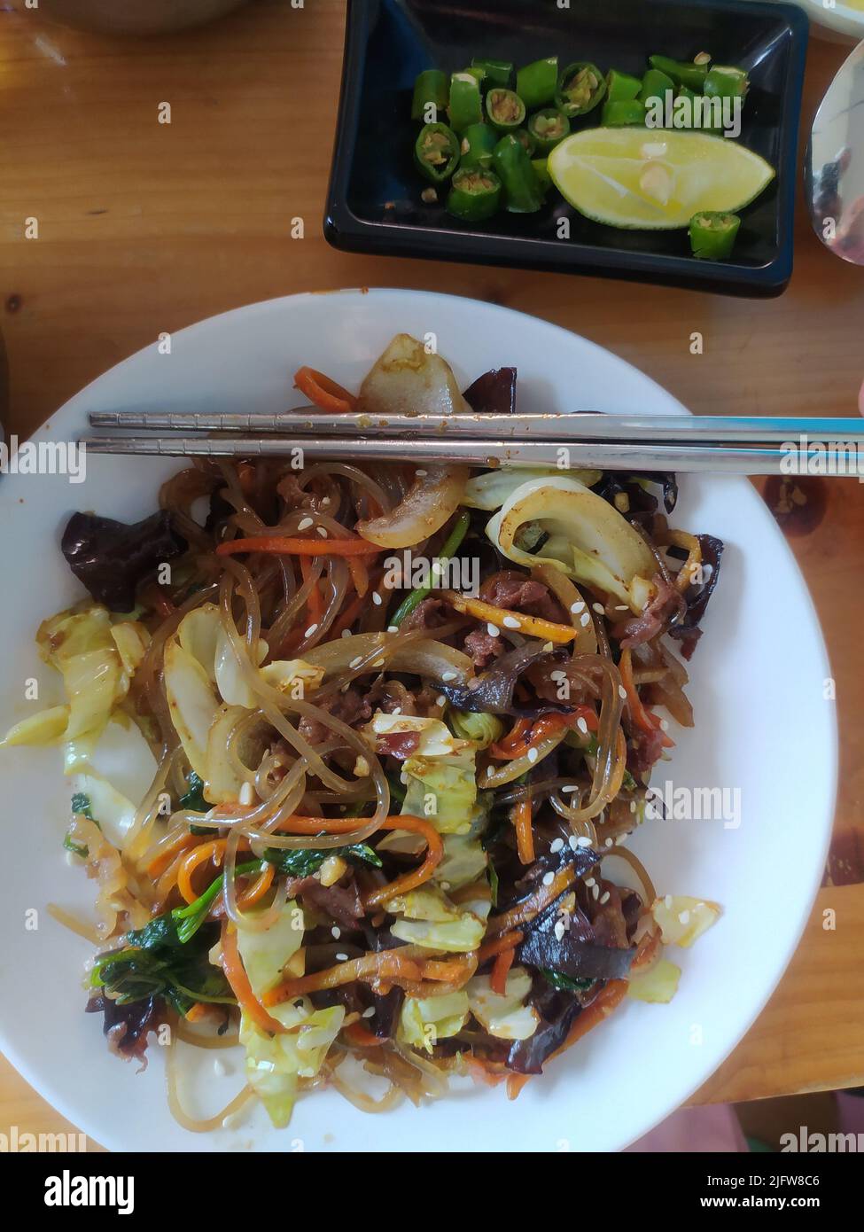Japchae with carrots and sesame seeds in the white plate on the table ...