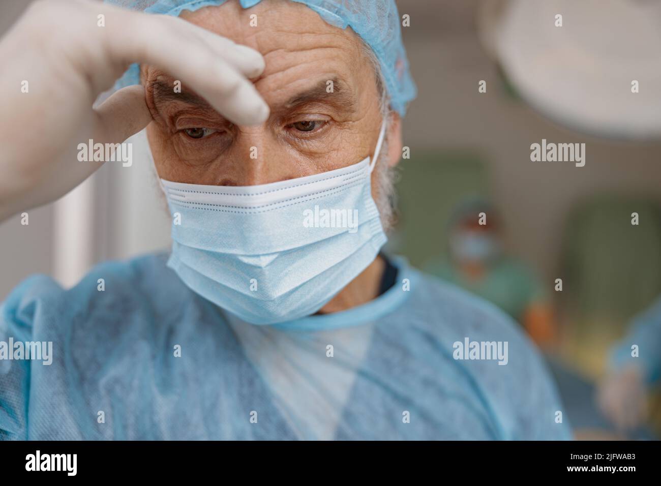 Close up of tired surgeon in mask standing in operating room after ...