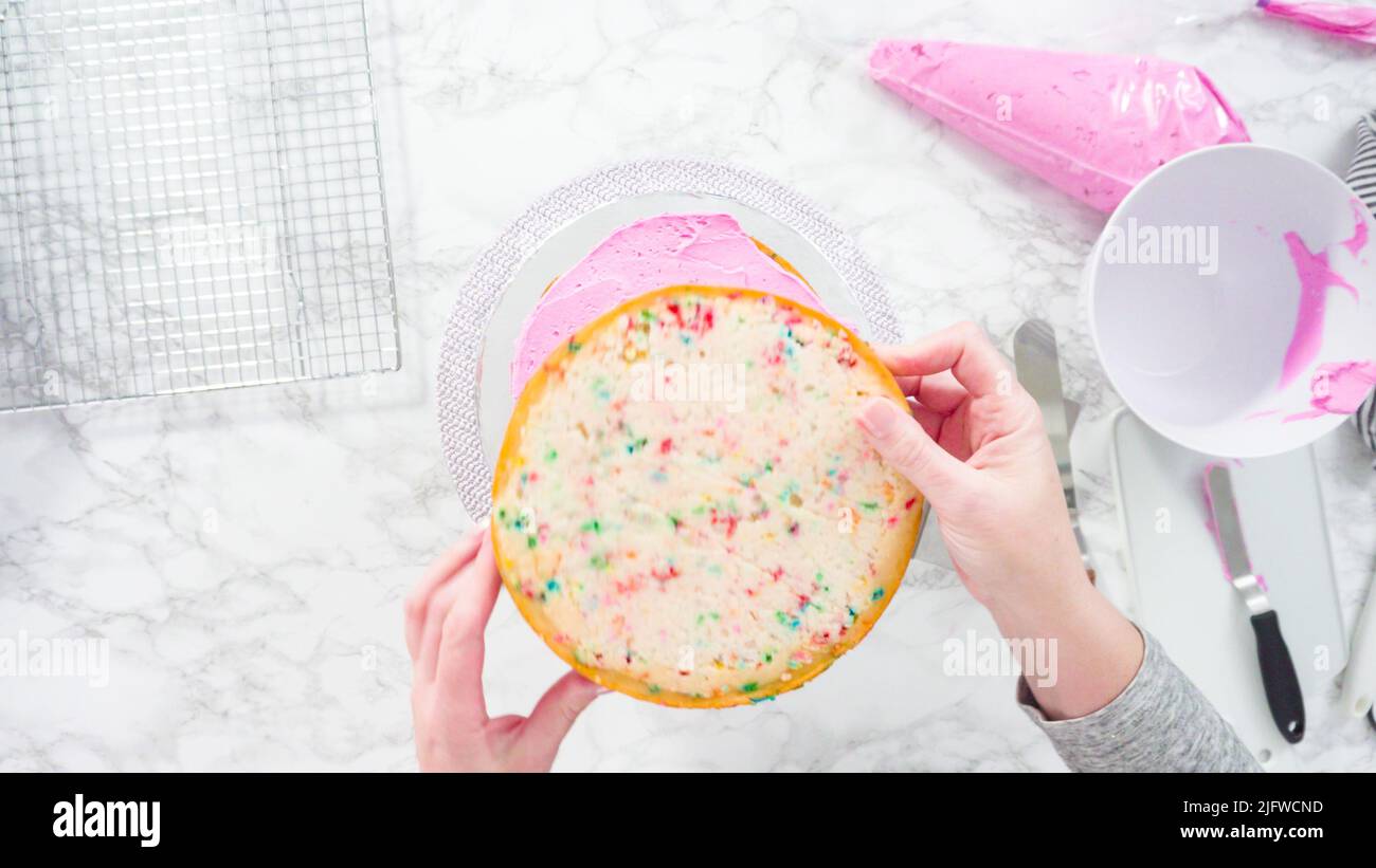 Flat lay. Step by step. Frosting round funfetti cake layers with pink ...