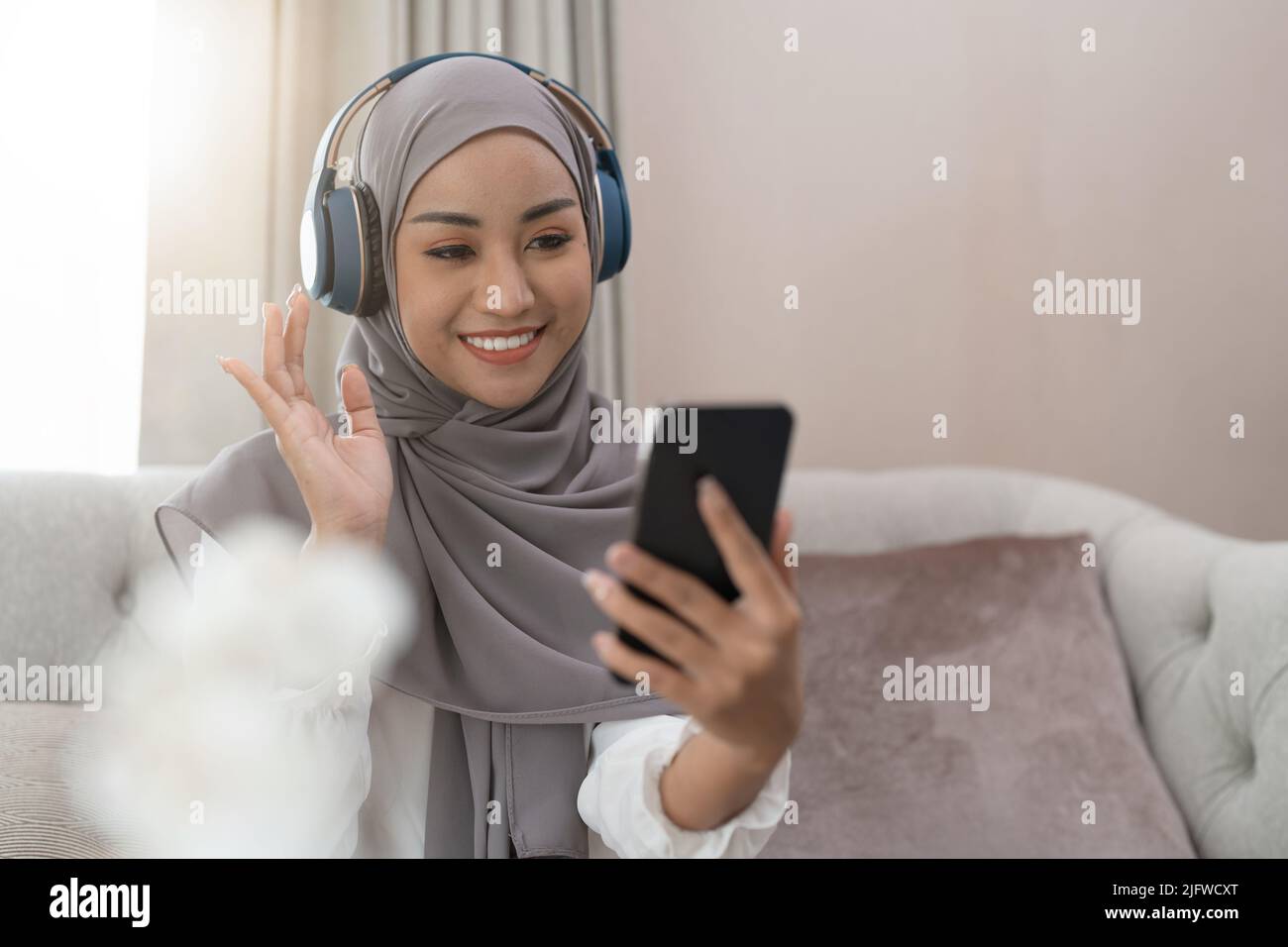Muslim woman sitting on sofa and video conference calling on mobile ...
