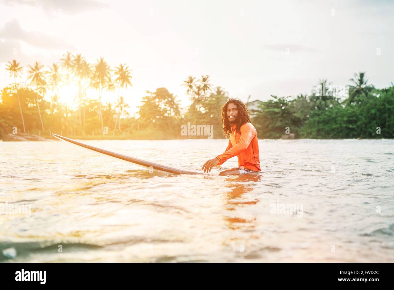 Black long-haired teen man floating on long surfboard, waiting for a ...