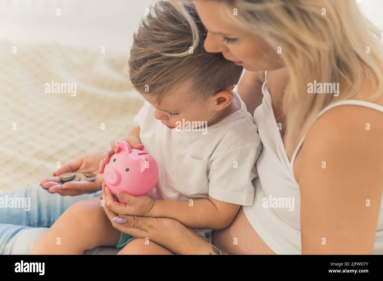 Proud young caucasian mother learning her son how to use a piggy bank ...
