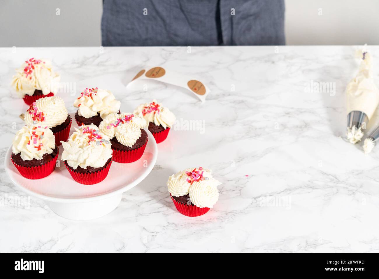 Piping white chocolate ganache frosting on top of red velvet cupcakes ...