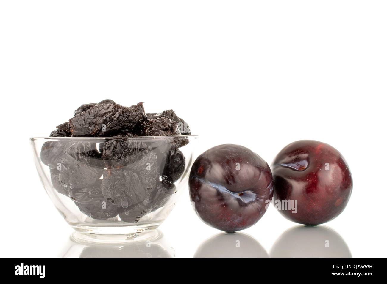 Two ripe fresh black plums and a few prunes in a glass bowl, close-up ...