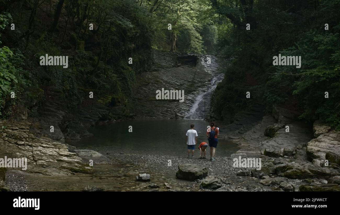 Family looks at waterfall in jungle. Creative. Family of tourists look ...