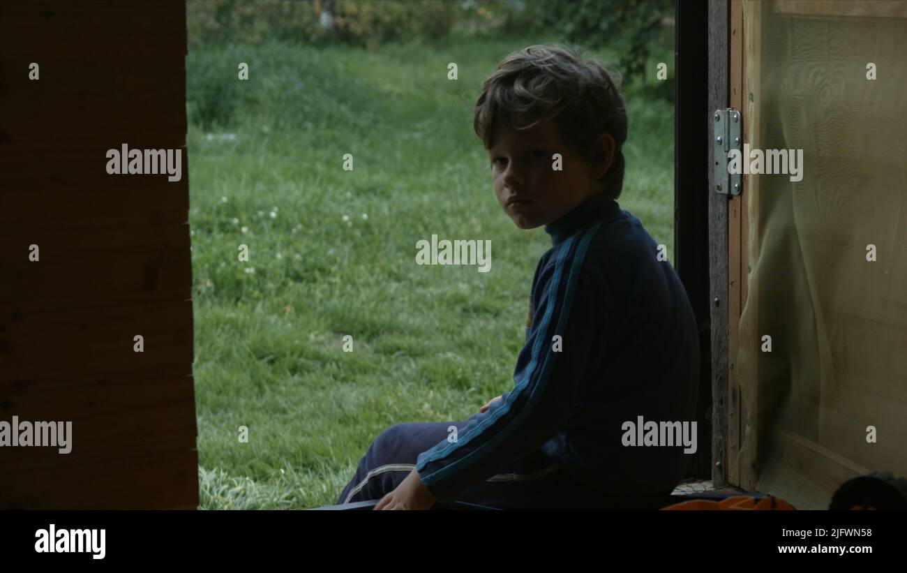 Beautiful boy is sitting on porch of house . Creative. Little boy is ...