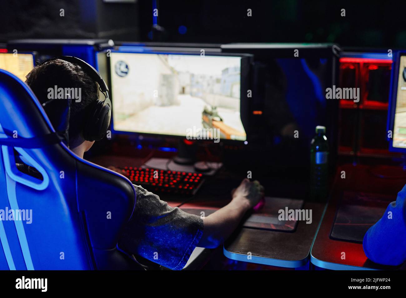 Back view of young man playing video game shooter in dark with ...