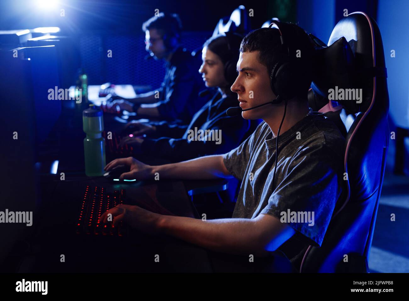 Side view portrait of young people playing video games in row at cyber ...