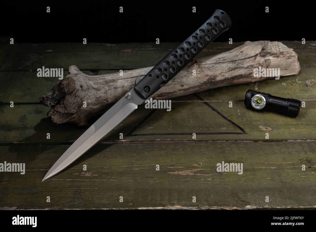 A large sharp knife and a dry wooden branch. Knife and flashlight ...