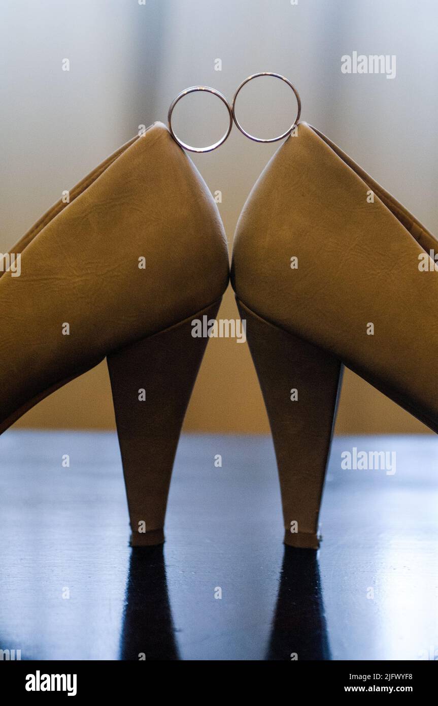 A vertical shot of a bride's shoe's hills with wedding rings among them ...
