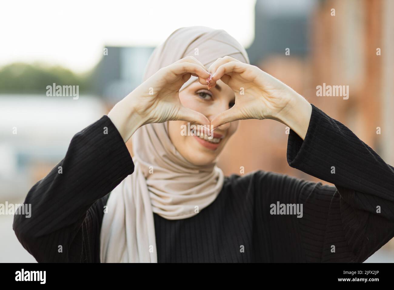 Smiling arabian muslim woman in hijab and black clothes posing on urban ...