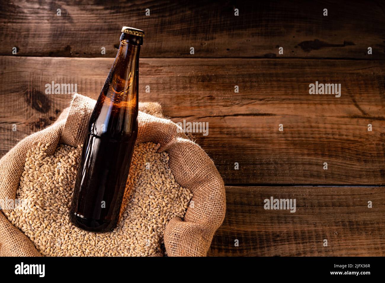 A bottle of dark beer in a bag of wheat. A beam of light falls on a ...