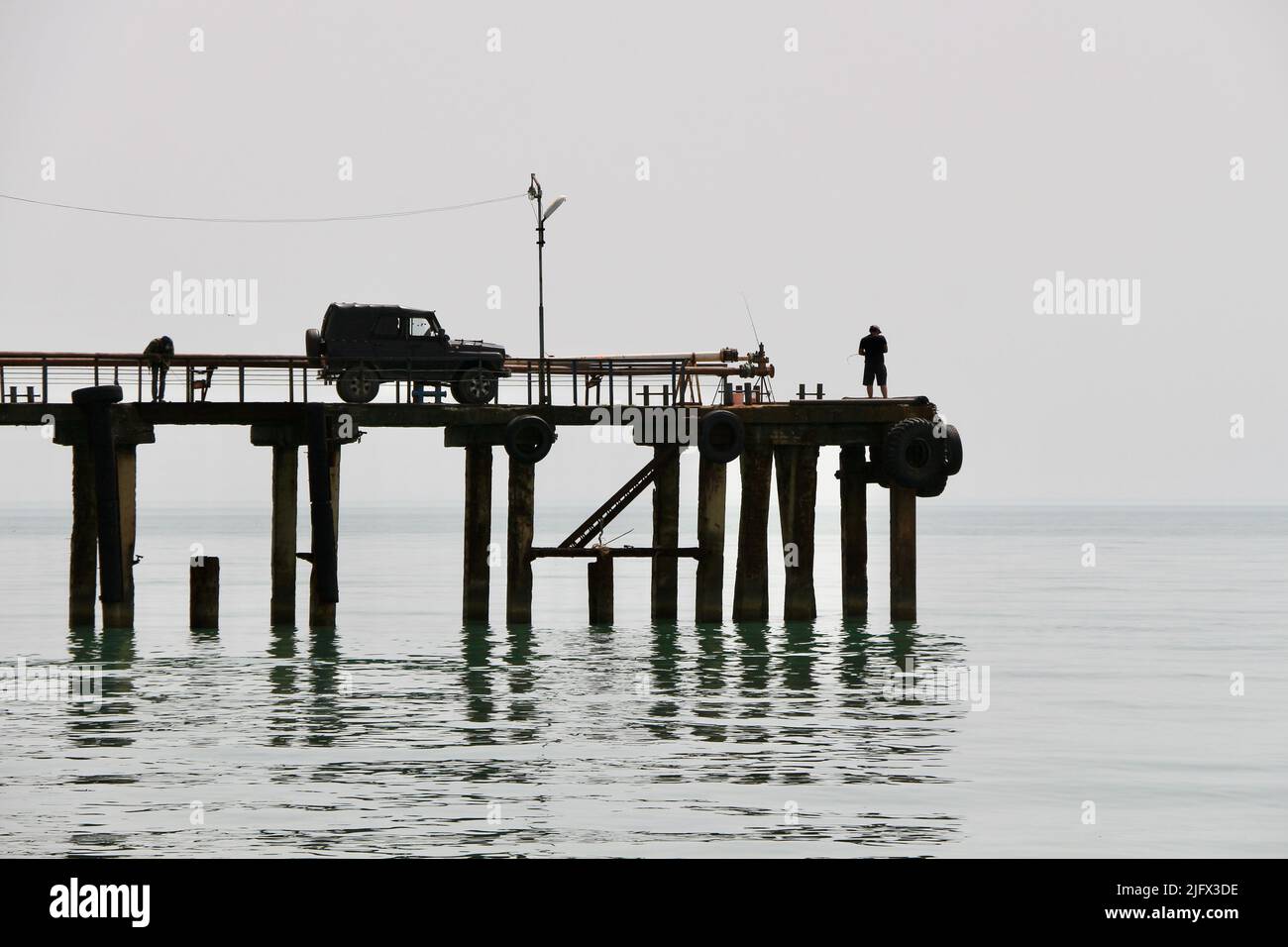A man standing on a bridge in the middle of the sea and catches fish ...