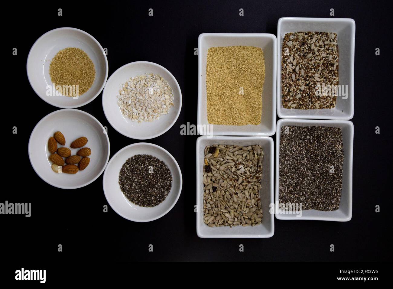 Dark background with white bowls contain healthy seeds for a vegan diet ...