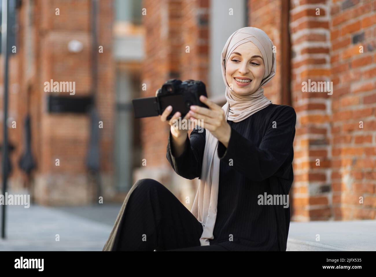 Young female muslim blogger in trendy clothes and hijab sitting on ...